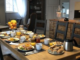 Mesa de café da manhã posta com diversos pratos, incluindo frutas, pão e bebidas.