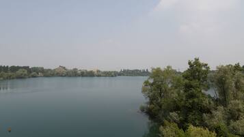 Um lago tranquilo com um pequeno barco, rodeado por árvores densas e um edifício ao longe.