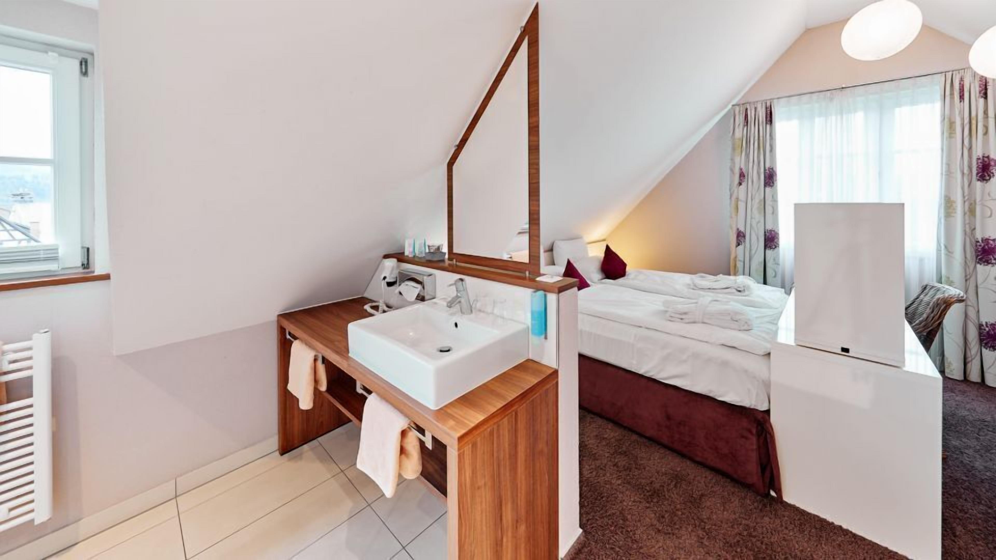 Quarto moderno com toucador de madeira, um espelho grande, cama branca e vista para a cidade pela janela.