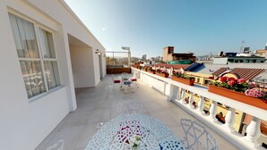 Terraço no telhado com área de refeições, plantas em vasos e vista para a paisagem urbana.