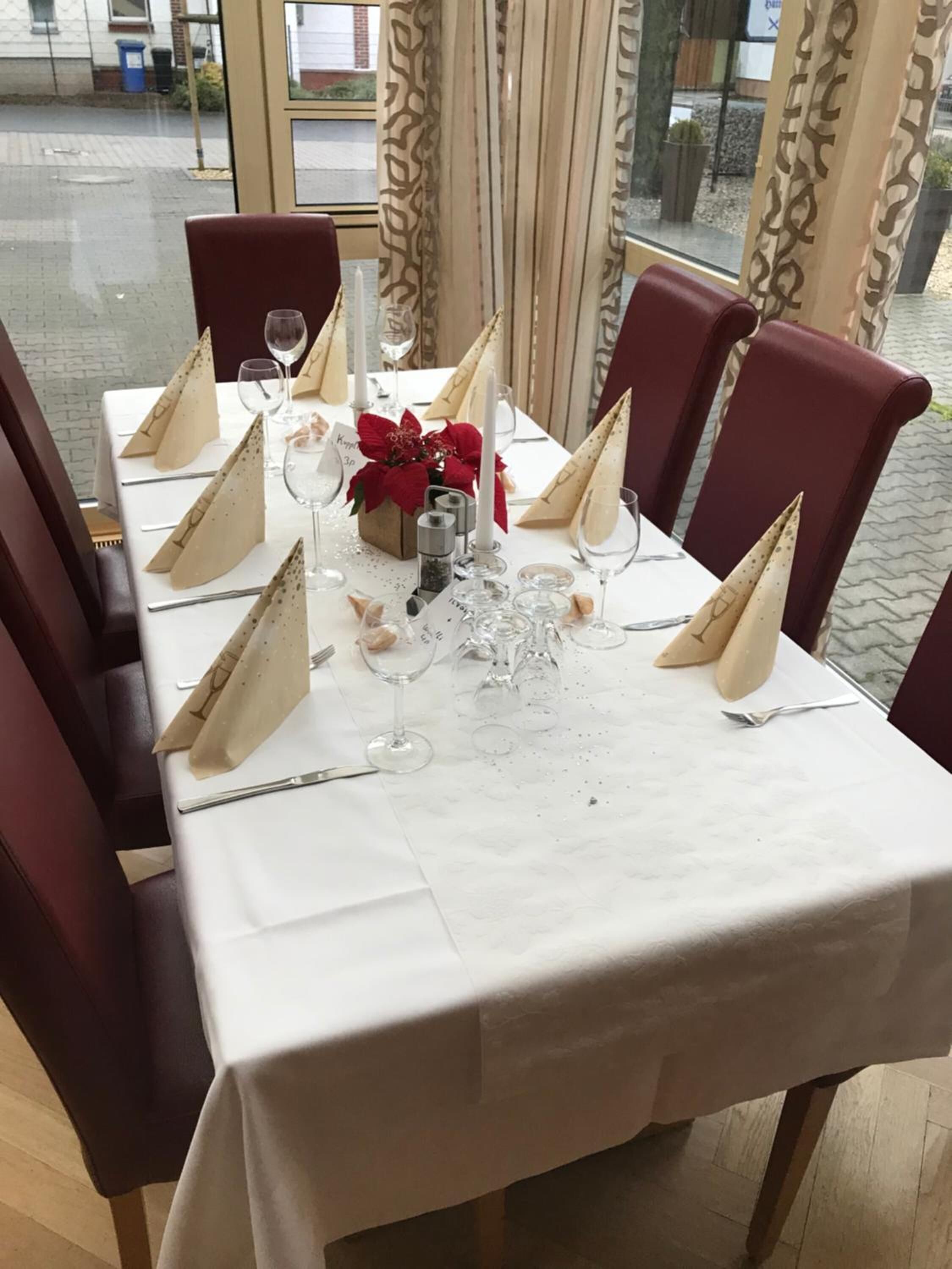 Mesa de jantar posta com toalha branca, cadeiras vermelhas e um arranjo floral vermelho como peça central.
