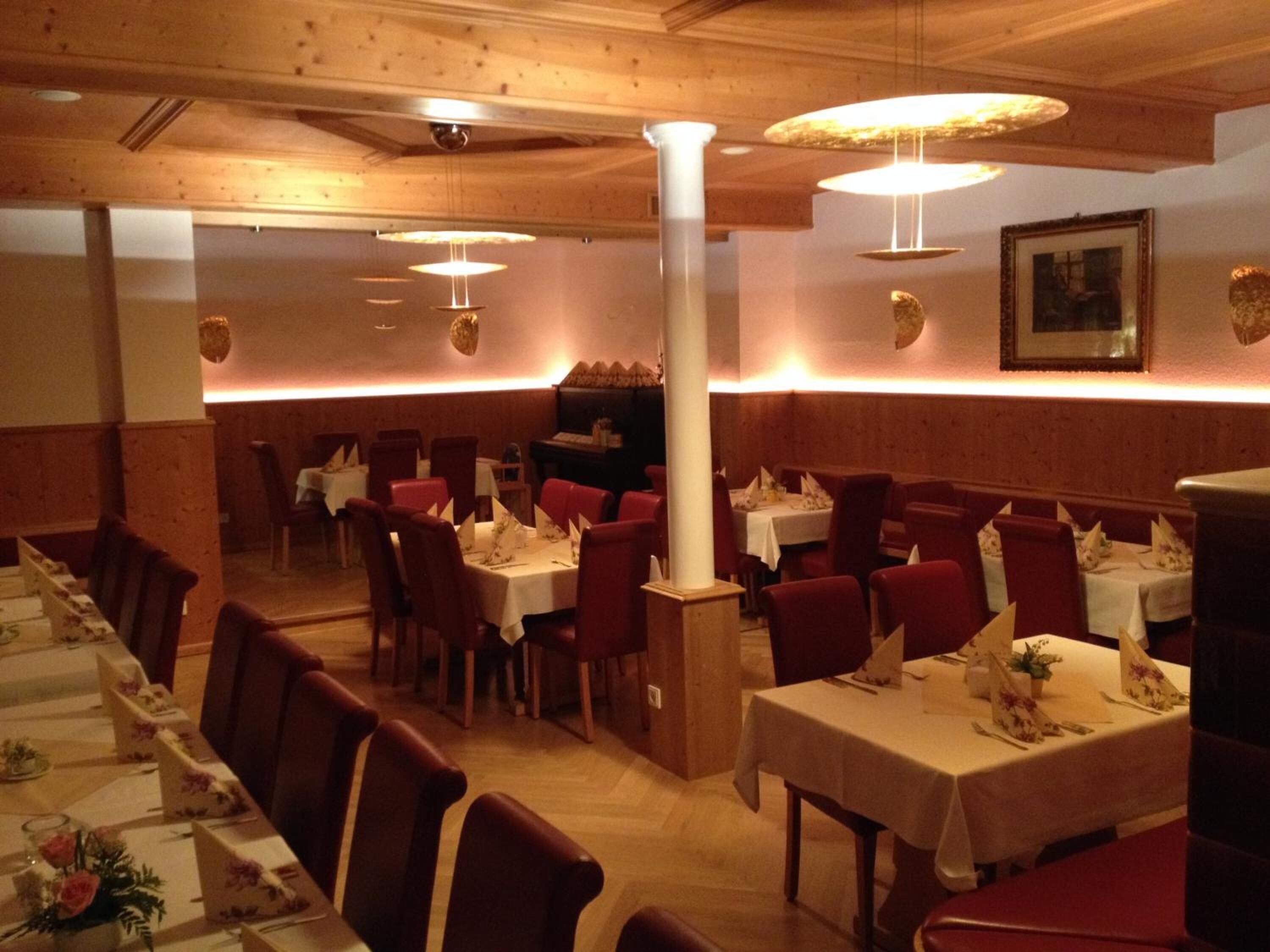 Um restaurante com painéis de madeira, mesas com toalhas brancas e cadeiras vermelhas, e iluminação pendente.