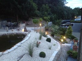Um jardim arborizado com lago, área de estar e plantas em vasos.