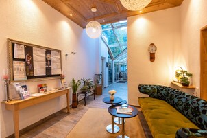 Um interior acolhedor com um banco de madeira, um sofá verde, uma pequena mesa com um vaso e um mural com diversos avisos.