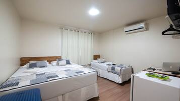 Quarto de hotel com duas camas, uma escrivaninha com um laptop, ar condicionado e um frigorífico.