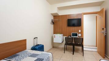 Quarto de hotel com cama, escrivaninha com computador, televisão, mini-geladeira e mala.