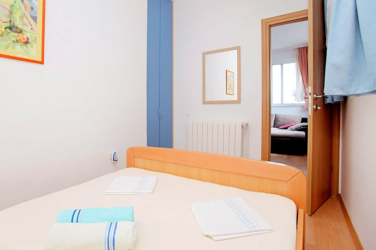Um quarto com cama, radiador, porta que dá para outro cômodo e um quadro na parede.