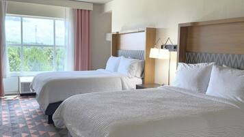 Quarto de hotel com duas camas, uma janela grande com vista, piso estampado e mesa de cabeceira com abajur.
