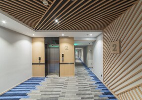 Corredor moderno de hotel com teto de madeira, carpete estampado e placa com o número 2 na parede.