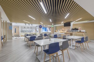 Uma cafeteria moderna com várias mesas e cadeiras, uma área de cozinha e uma televisão de tela plana na parede.