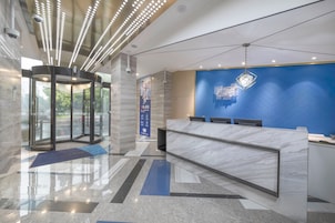 Um hall de hotel moderno com uma recepção de mármore, parede com padrão azul em chevron e porta giratória.