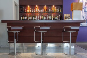 Uma área de bar com três banquetas e uma prateleira com diversas garrafas de bebidas.