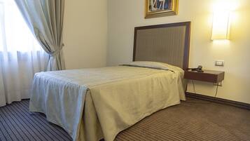 Quarto de hotel com uma cama, mesa de cabeceira, abajur e um quadro na parede.