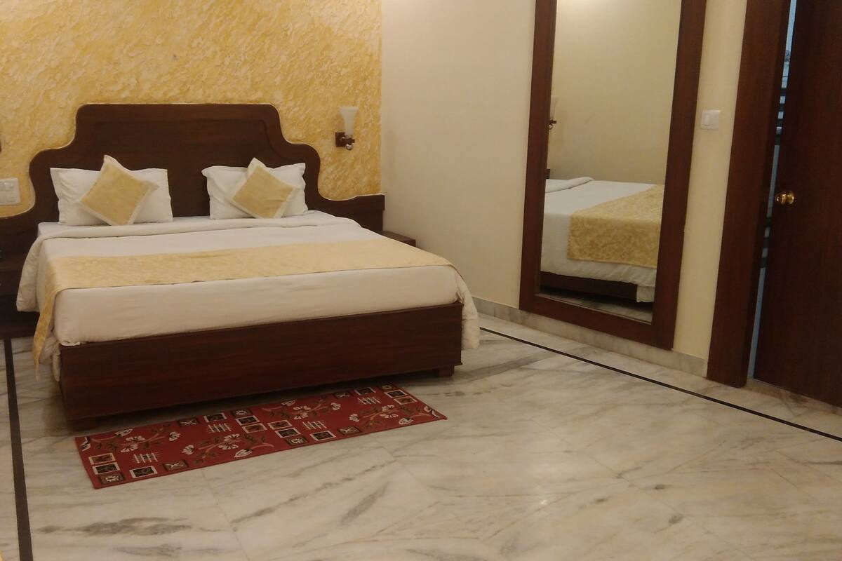 Quarto com cama, tapete vermelho e espelho refletindo uma cama.
