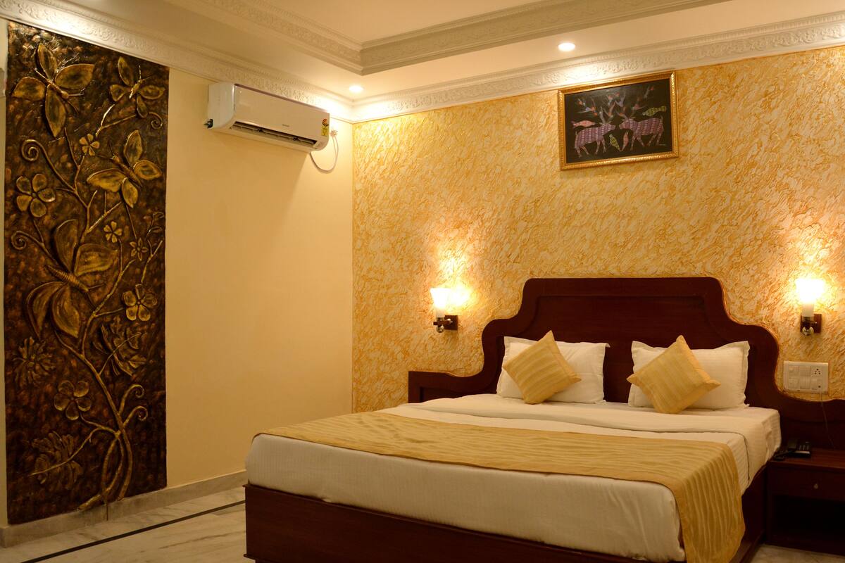 Quarto de hotel com uma cama grande, duas mesas de cabeceira, um aparelho de ar condicionado e um painel decorativo na parede.