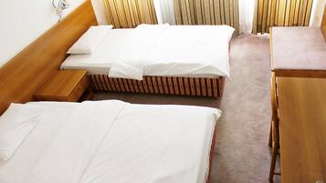 Quarto de hotel com duas camas de solteiro, uma mesinha de cabeceira de madeira, um armário de madeira e uma pequena mesa.