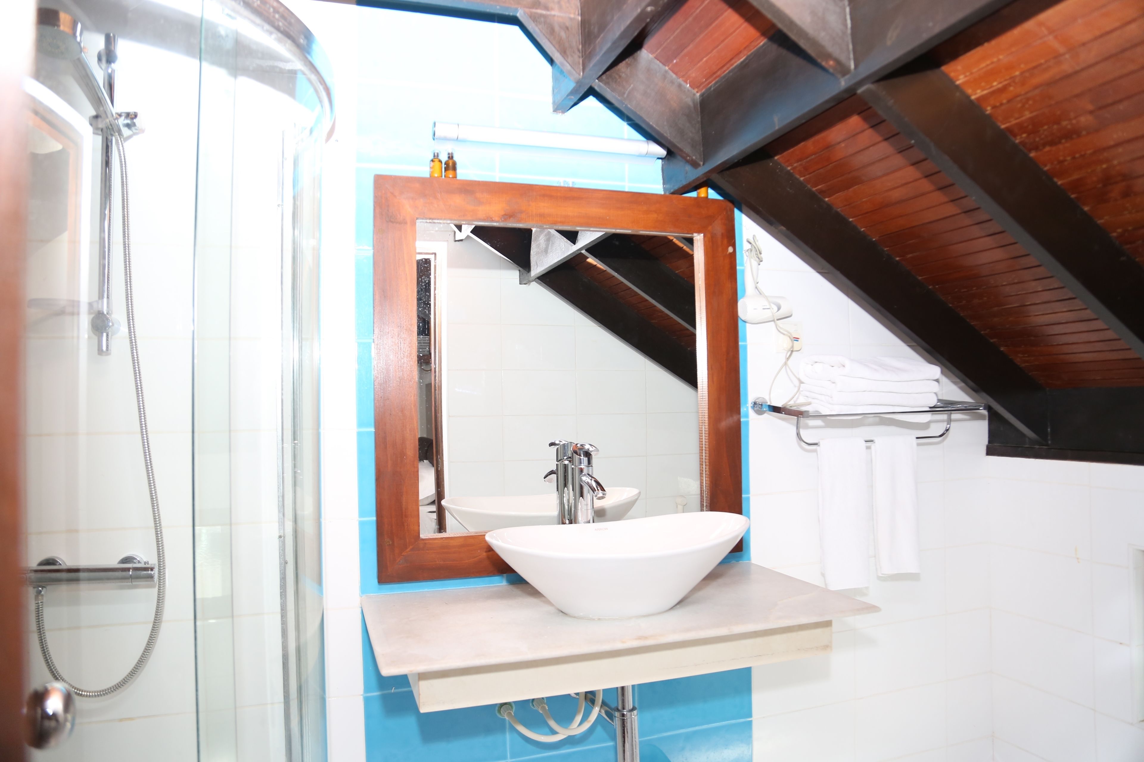Casa de banho com chuveiro em cabine de vidro, lavatório branco com toucador de madeira e espelho com moldura de madeira.