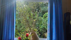 Uma janela com cortinas azuis, uma mesa branca, um vaso com flores e um abajur.