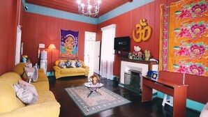 Uma sala de estar com um sofá amarelo, lareira, televisão e um grande tapeçaria floral.