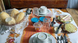 Mesa de pequeno-almoço posta com pão, ovos e diversos itens para pequeno-almoço sobre toalha de mesa xadrez.