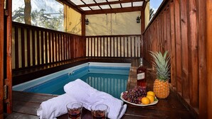 Um deck de madeira com piscina, uma toalha, copos e um prato de frutas.