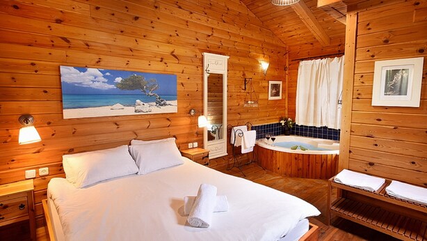 Quarto de cabana de madeira com uma cama grande, uma banheira e uma pintura com uma paisagem praiana.