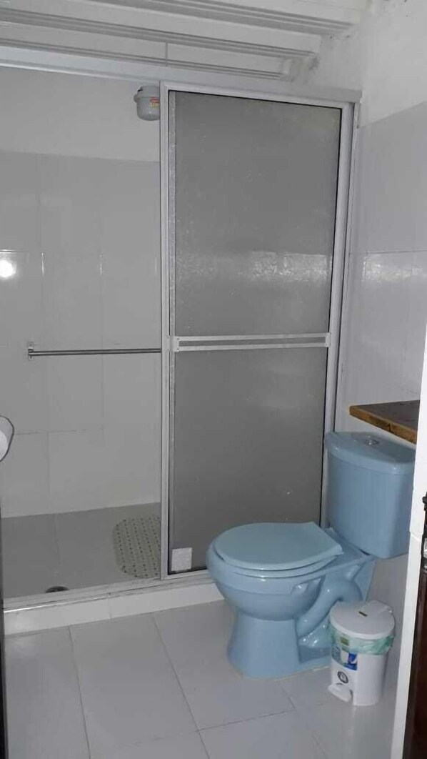 Casa de banho com cabine de chuveiro, sanita e um cesto de lixo.