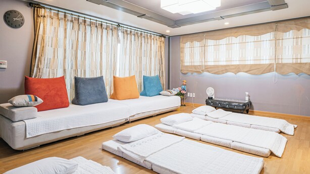 Quarto de hotel com várias camas, um relógio na parede e uma janela com cortinas.