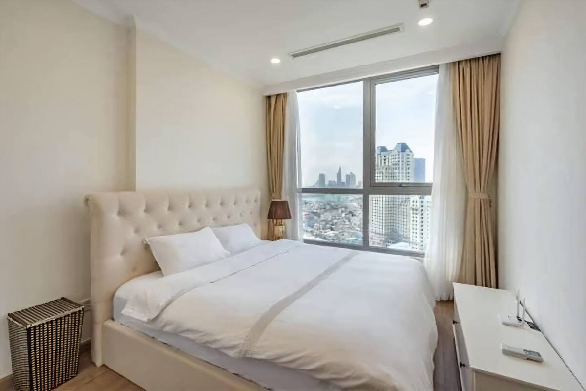 Quarto de hotel moderno com uma cama grande, uma escrivaninha e vista para a cidade pela janela.