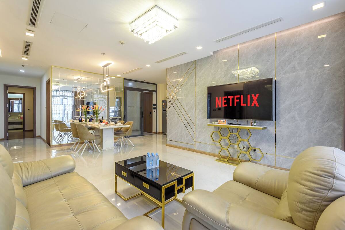 Uma sala de estar moderna com uma grande televisão de tela plana, sofás de couro, uma mesa de centro de vidro e uma área de refeições com cadeiras e mesa.