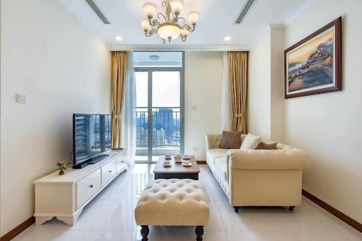 Uma sala de estar moderna com uma televisão de tela plana, um sofá bege, uma mesa de centro e um lustre.