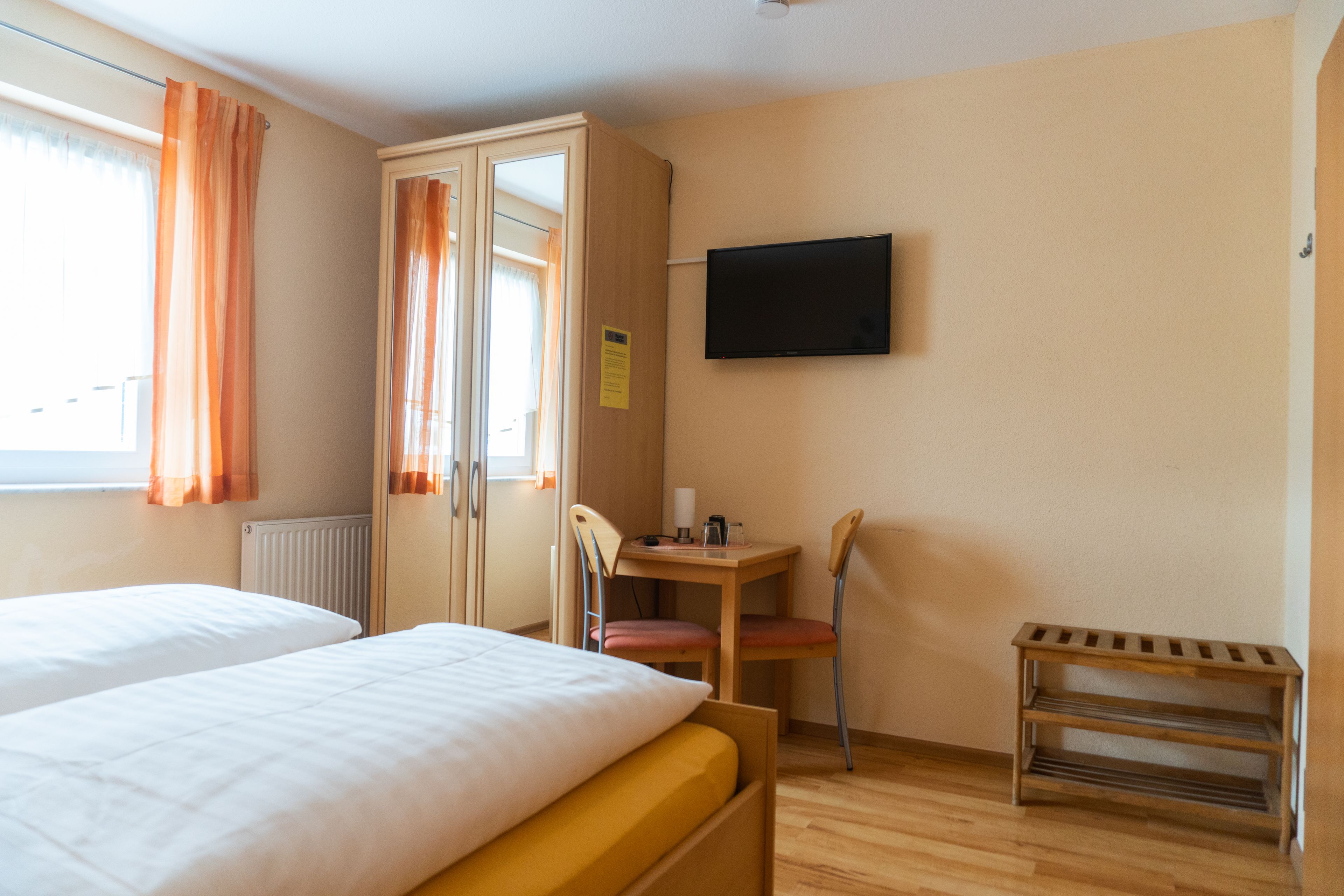 Quarto de hotel com duas camas, uma escrivaninha, uma cadeira, uma televisão e um radiador.