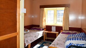 Um quarto pequeno e acolhedor com duas camas de solteiro, uma mesa de madeira e uma janela com cortinas.