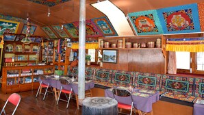 Uma hospedaria tradicional com móveis de madeira, tapeçarias coloridas e diversos objetos em prateleiras.