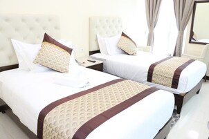 Quarto de hotel com duas camas, cada uma com cabeceira estofada, roupa de cama branca e almofadas decorativas castanhas.