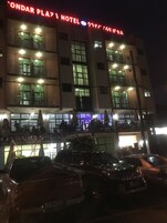 Um hotel com vários andares, sinalização iluminada, área de estar externa e estacionamento visível.