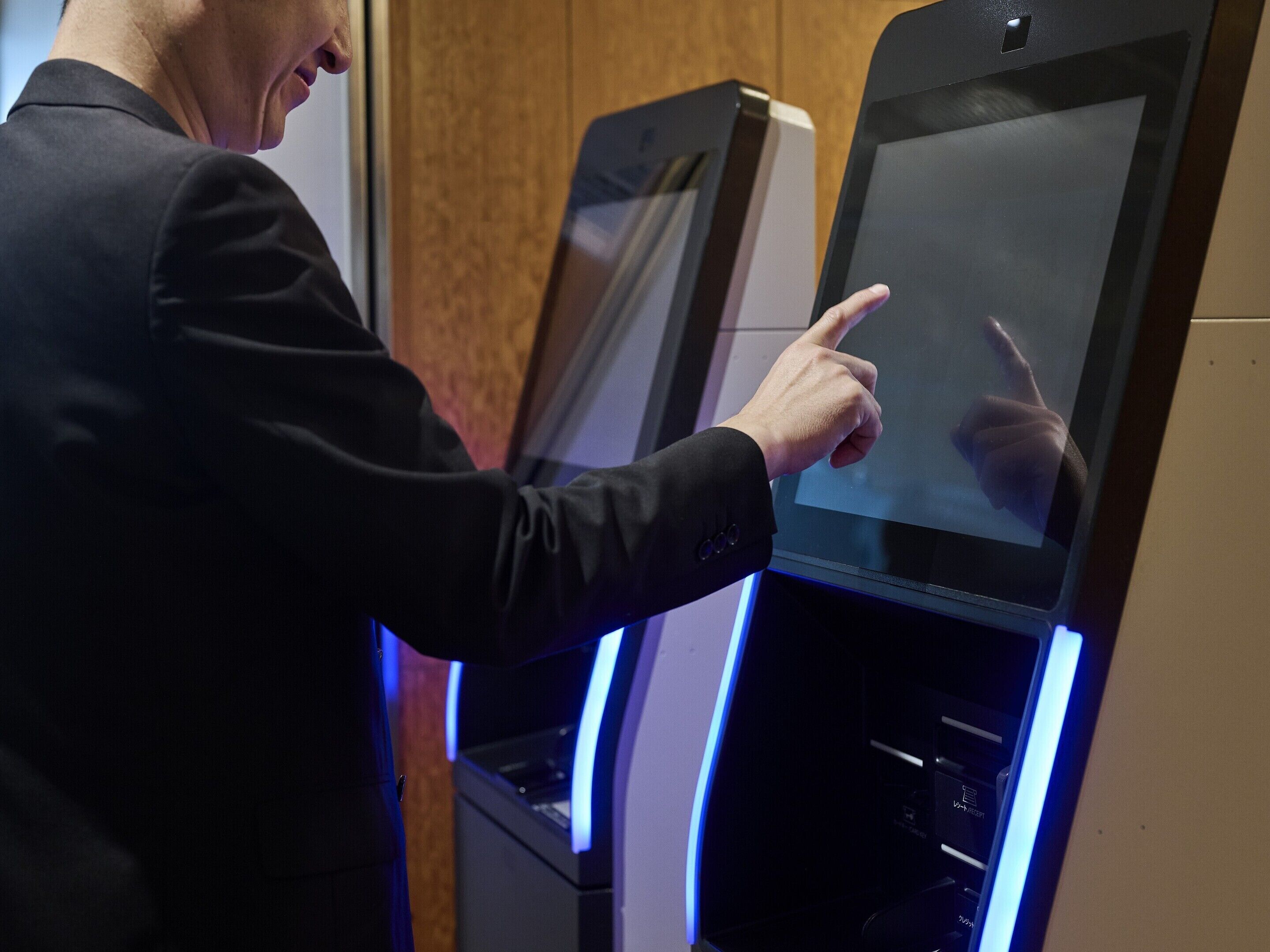 Uma pessoa interagindo com um quiosque touchscreen, provavelmente para registo de hóspedes ou obter informações.