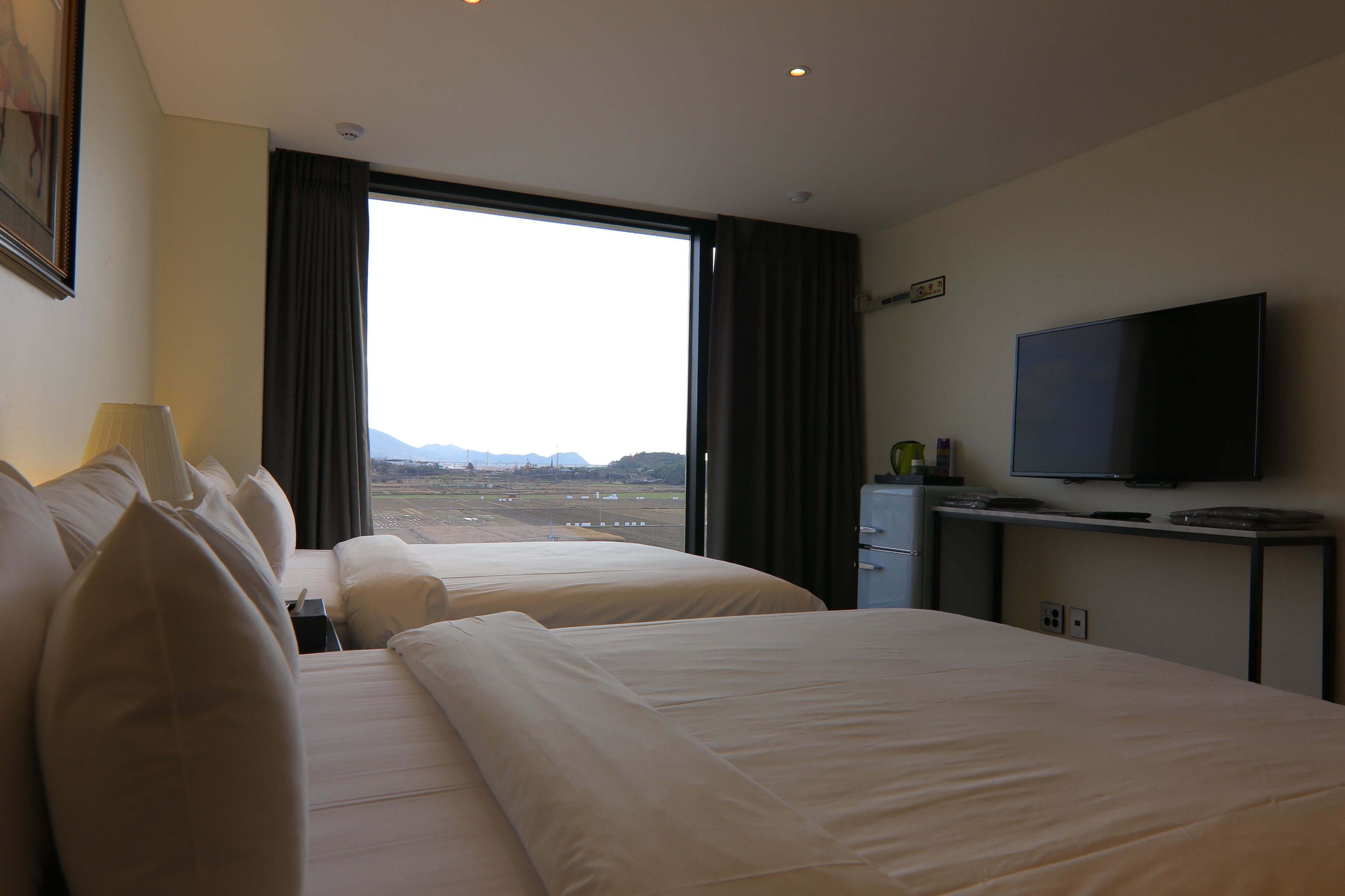 Quarto de hotel com duas camas, televisão e vista para a paisagem.