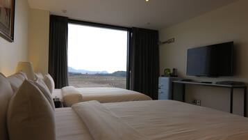 Quarto de hotel com duas camas, televisão e vista para a paisagem.