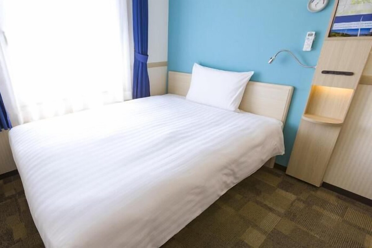 Quarto de hotel com cama, cortinas, relógio de parede, prateleira pequena e um mapa na parede.