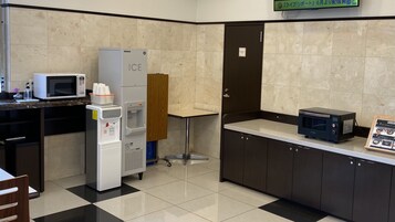 Uma cozinha compacta com micro-ondas, dispensador de gelo, bebedouro, pequena geladeira e torradeira preta.