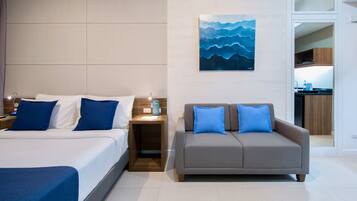 Quarto de hotel moderno com cama, sofá, mesa de cabeceira e um quadro na parede.