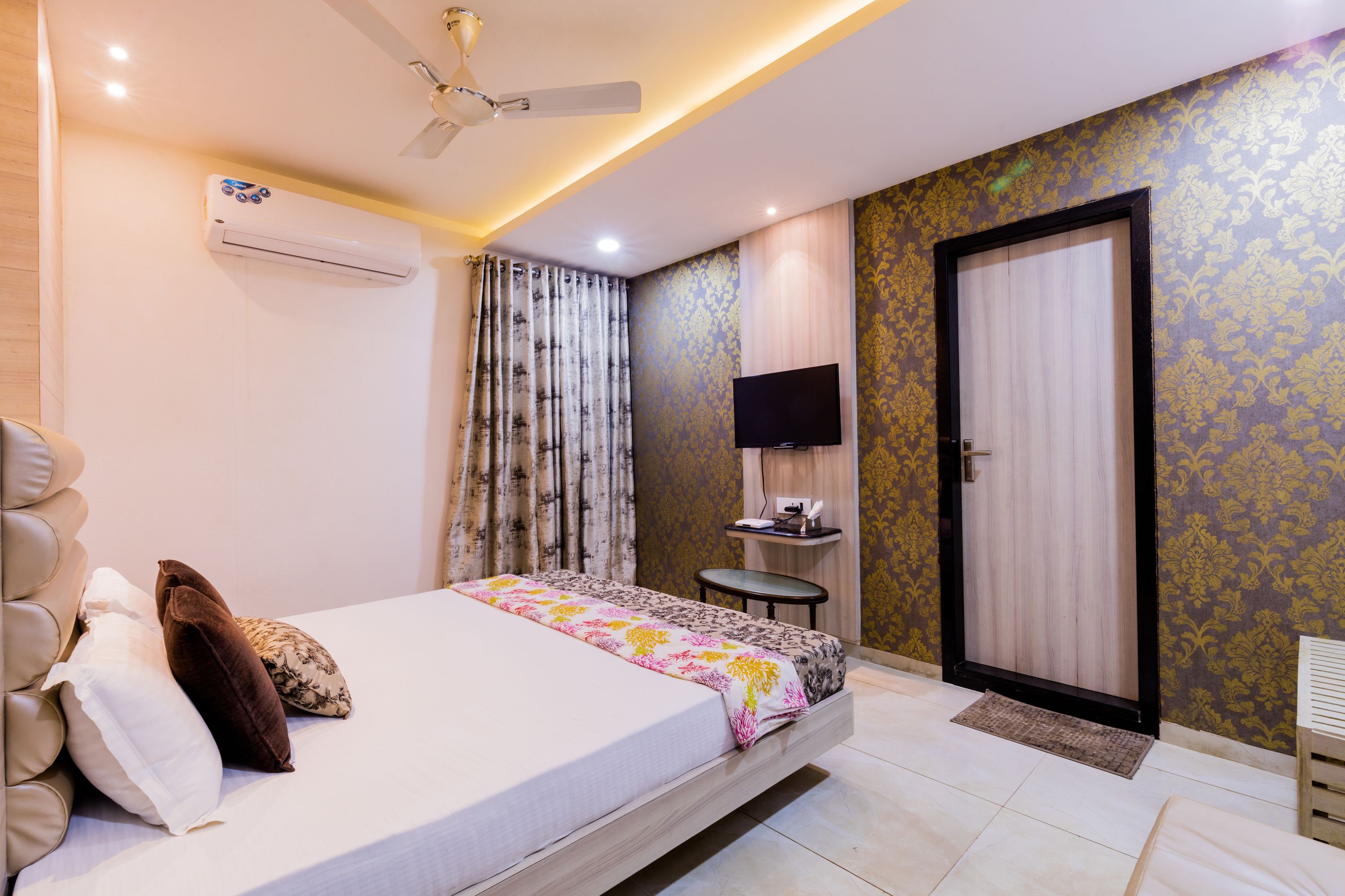 Quarto moderno com cama, ar condicionado, ventoinha no teto, televisão e uma porta.