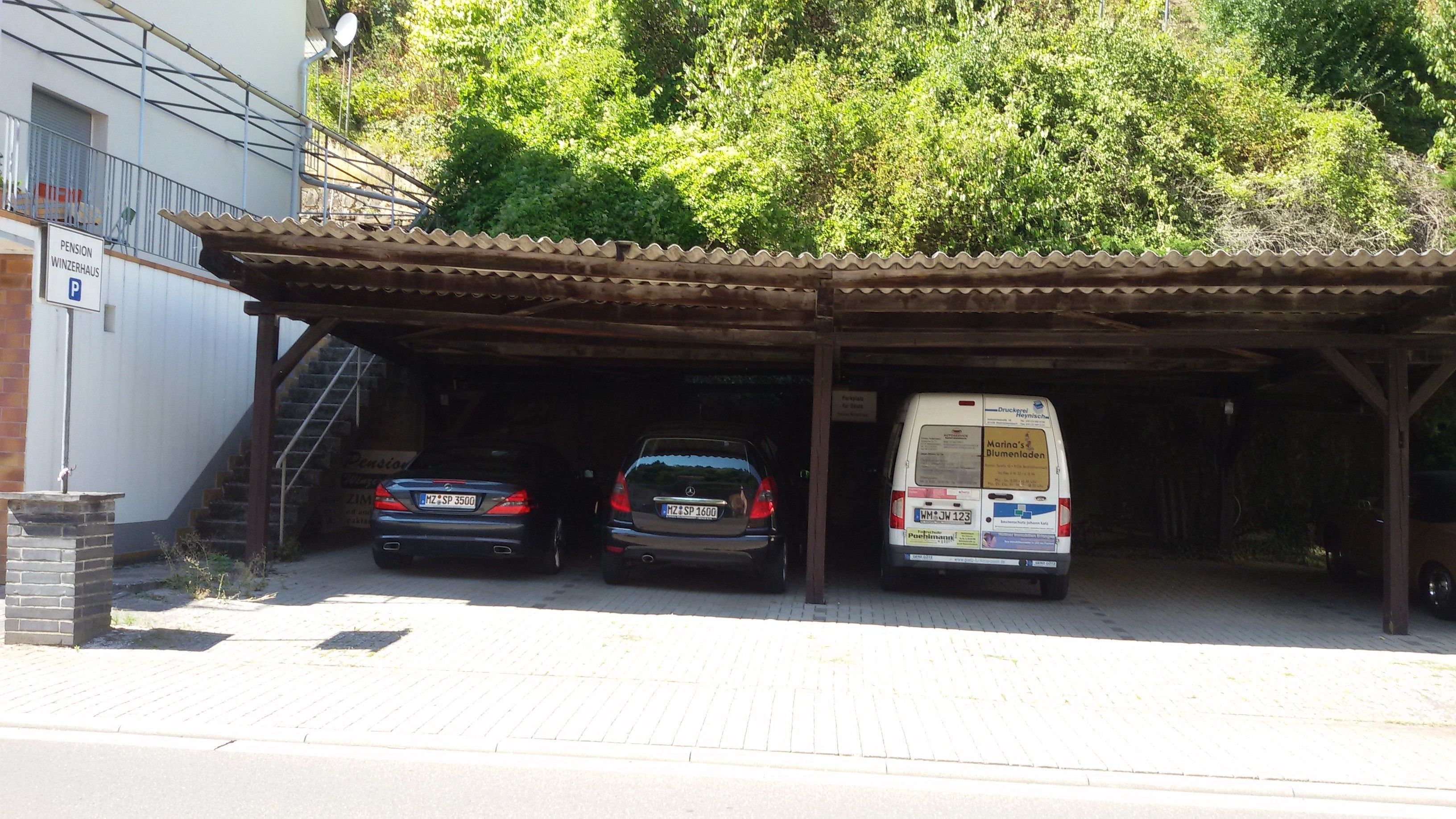 Área de estacionamento coberta com dois carros e uma van de entregas.