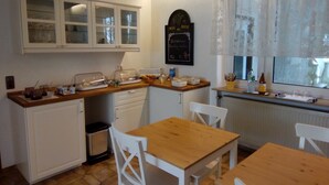 Cozinha compacta com armários brancos, bancada de madeira e área de refeições com cadeiras brancas e mesa de madeira.
