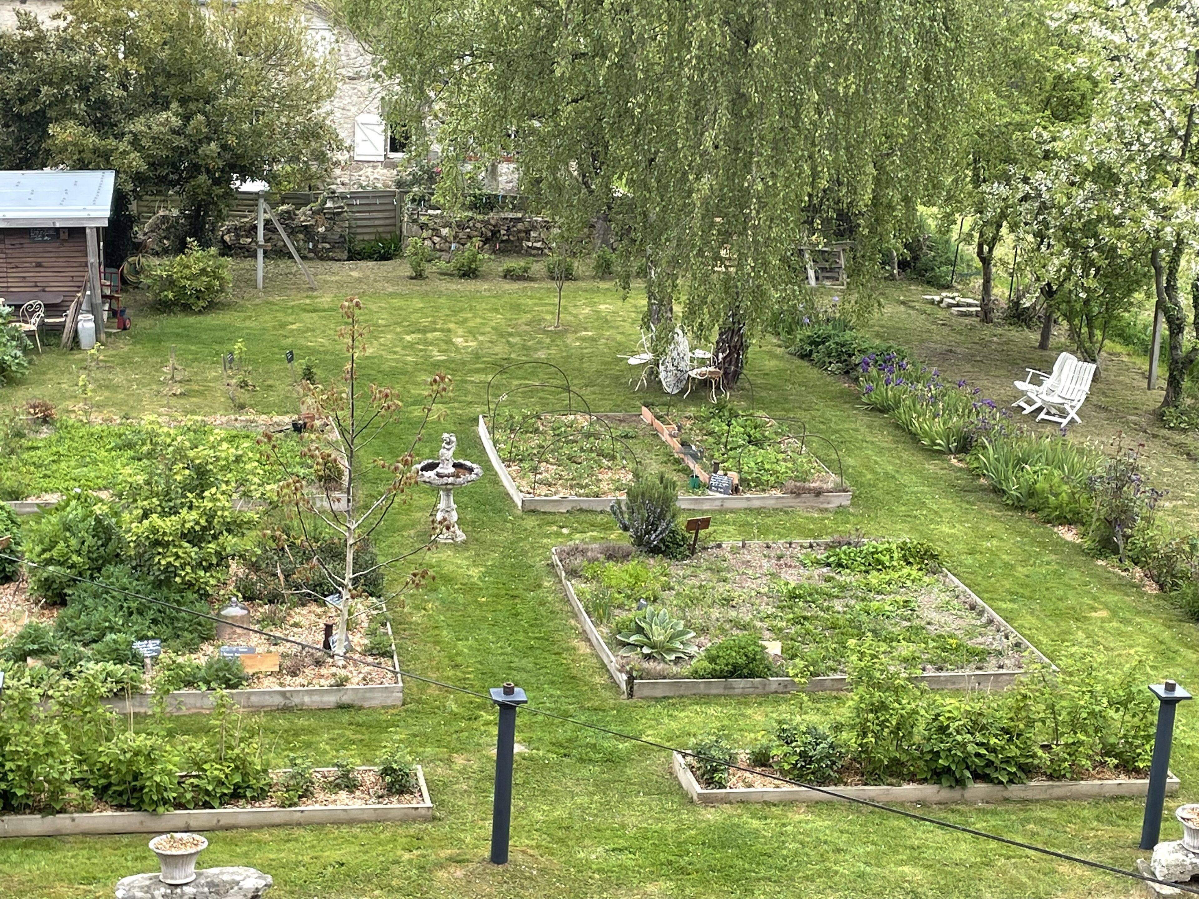 Um jardim bem cuidado com canteiros elevados, um bebedouro para pássaros e área de estar ao ar livre.