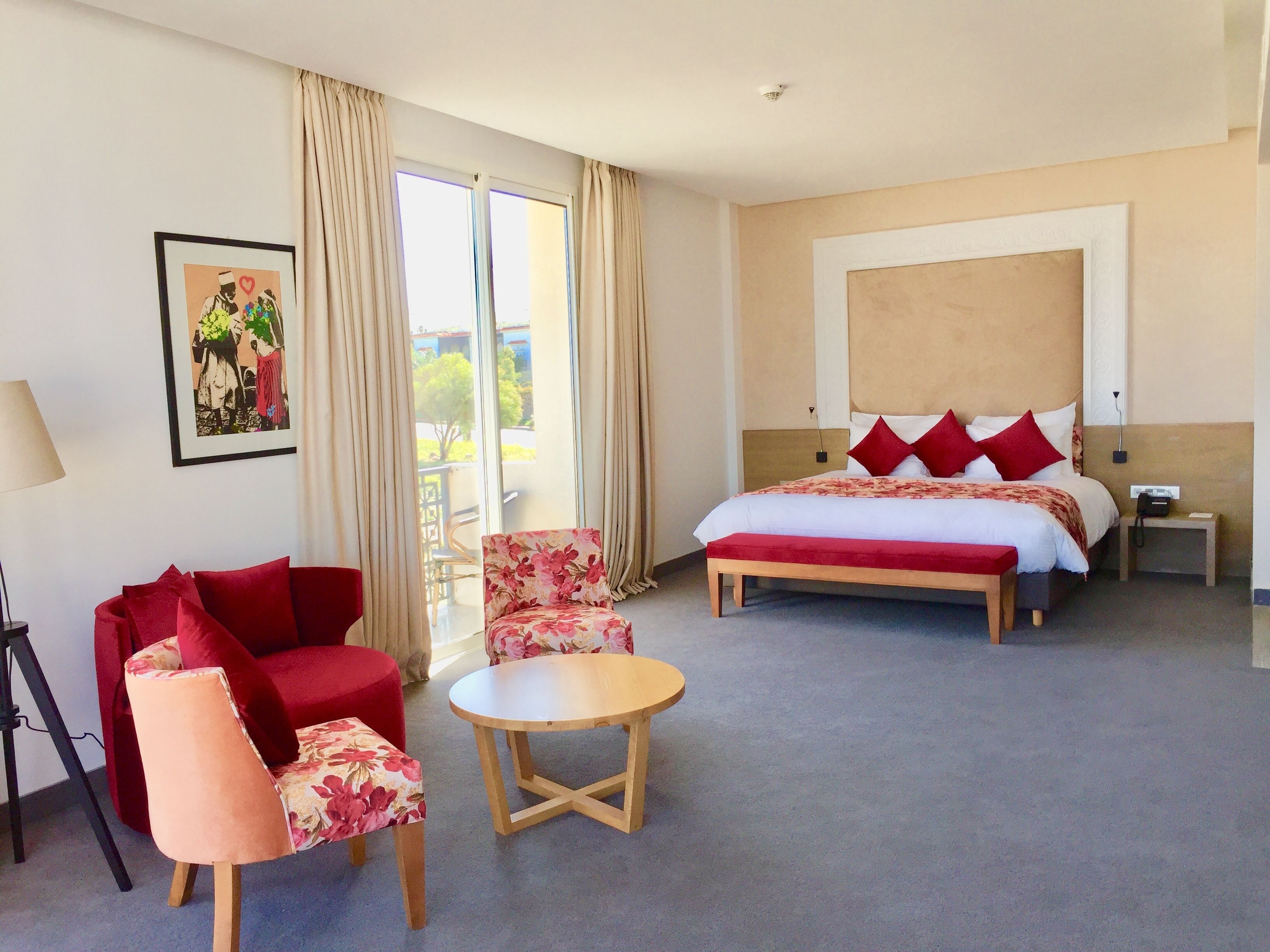 Quarto de hotel com cama, sofá, poltrona, mesinha e um quadro na parede.
