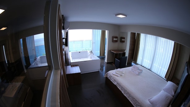 Quarto de hotel com uma cama grande, banheiro separado com banheira, uma pequena mesa de trabalho e vista para o mar.