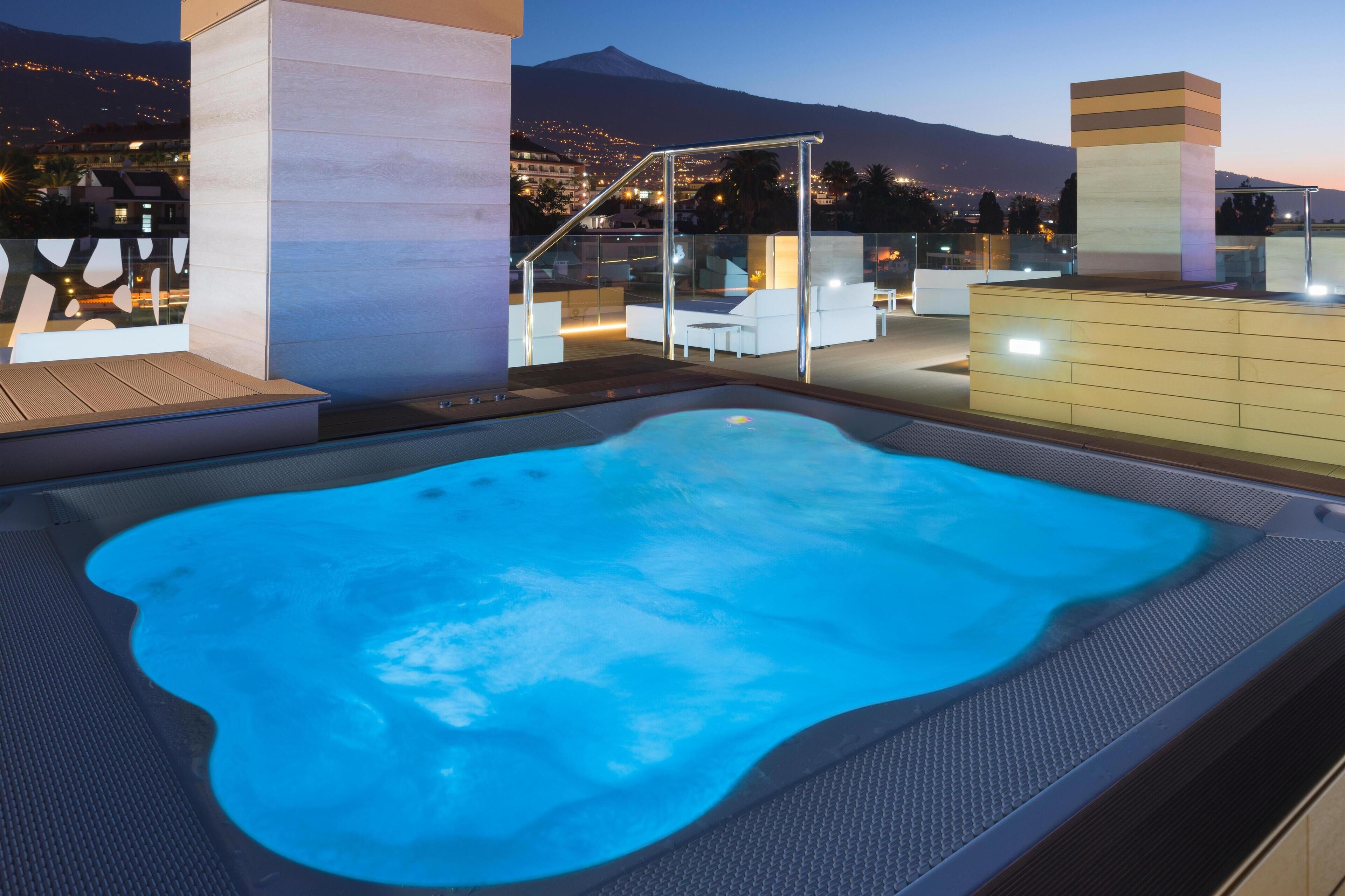 Uma banheira de hidromassagem com vista para uma montanha e luzes da cidade ao anoitecer.