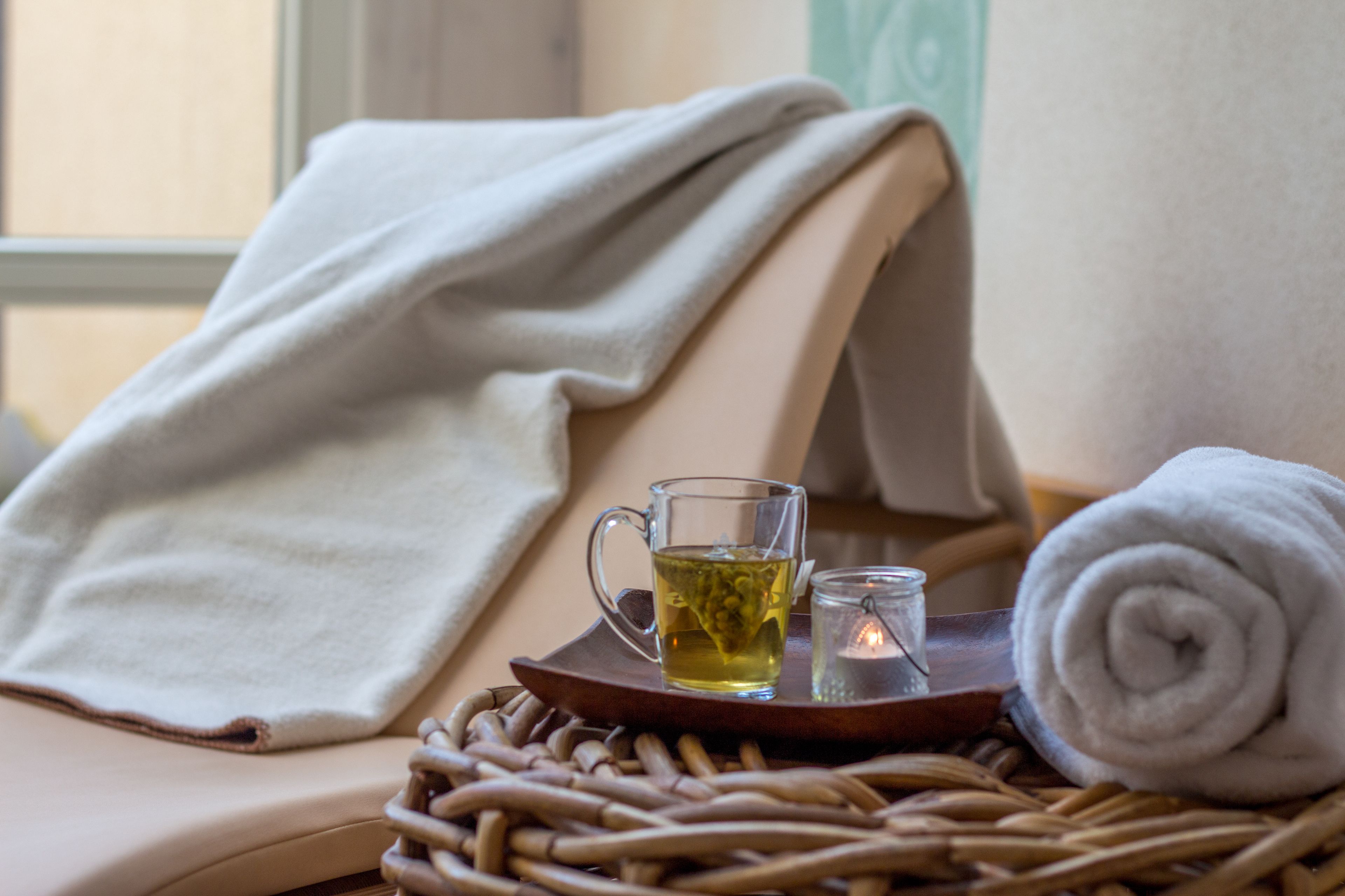 Ambiente de spa com cadeira de massagem, bandeja com chá, toalha enrolada e vela.
